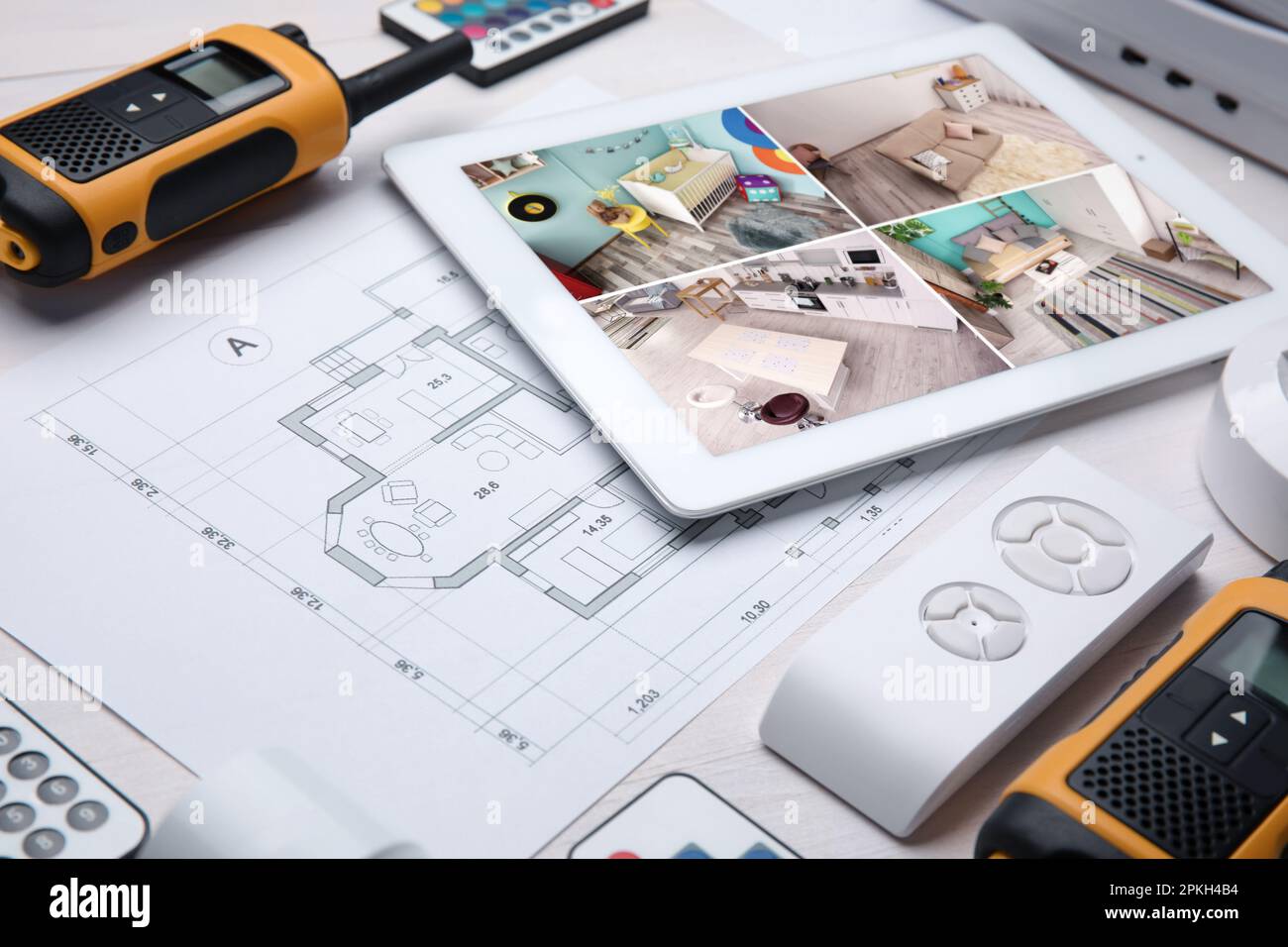 Tablet with view from CCTV cameras and building plan on white table ...