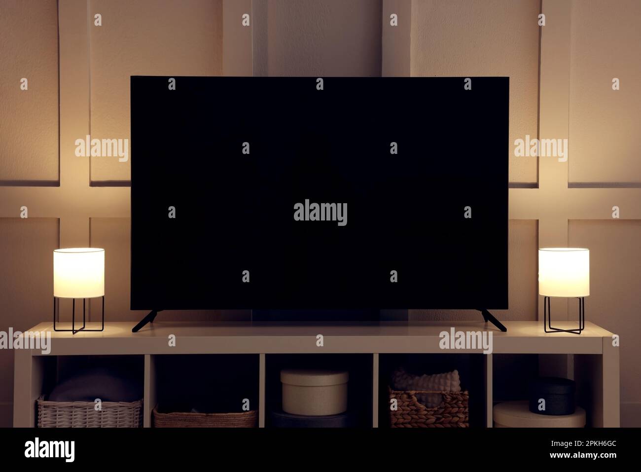 Modern TV and lamps on cabinet near white wall indoors. Interior design ...