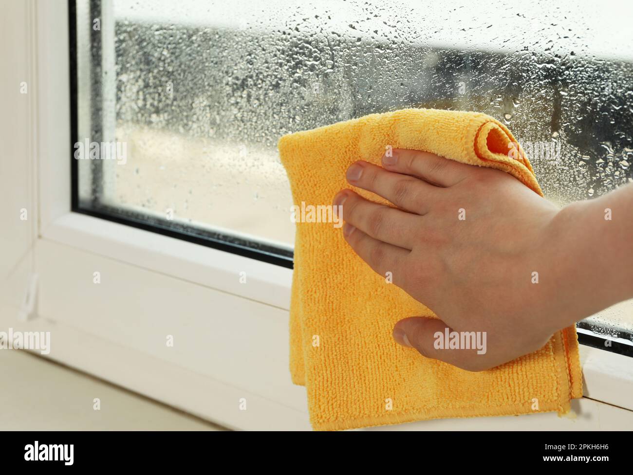 Woman wiping window glass with drops of condensate indoors, closeup ...