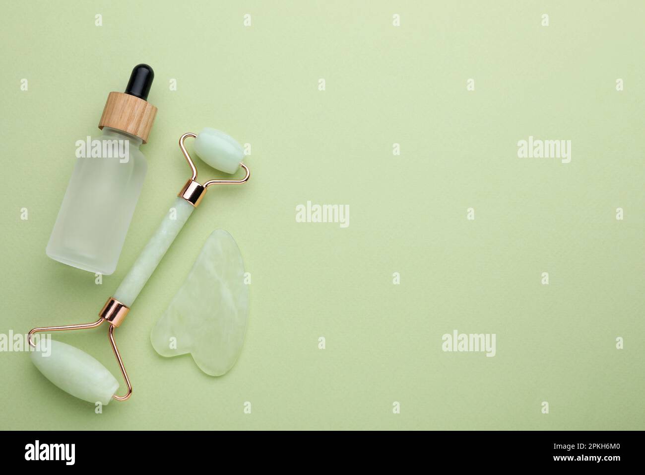 Jade gua sha tool , facial roller and bottle of serum on light green ...