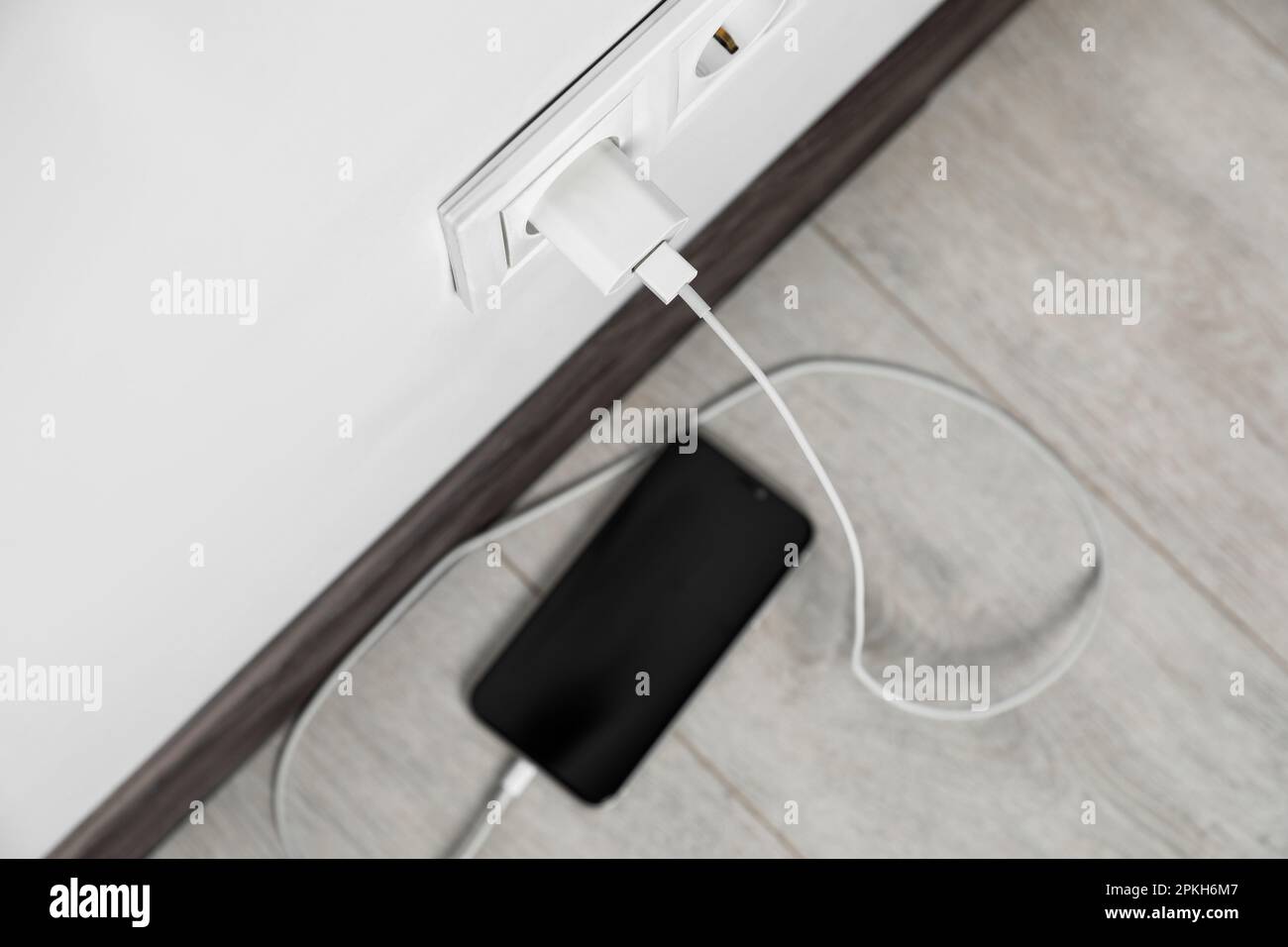 Modern smartphone charging from electric socket indoors, above view ...