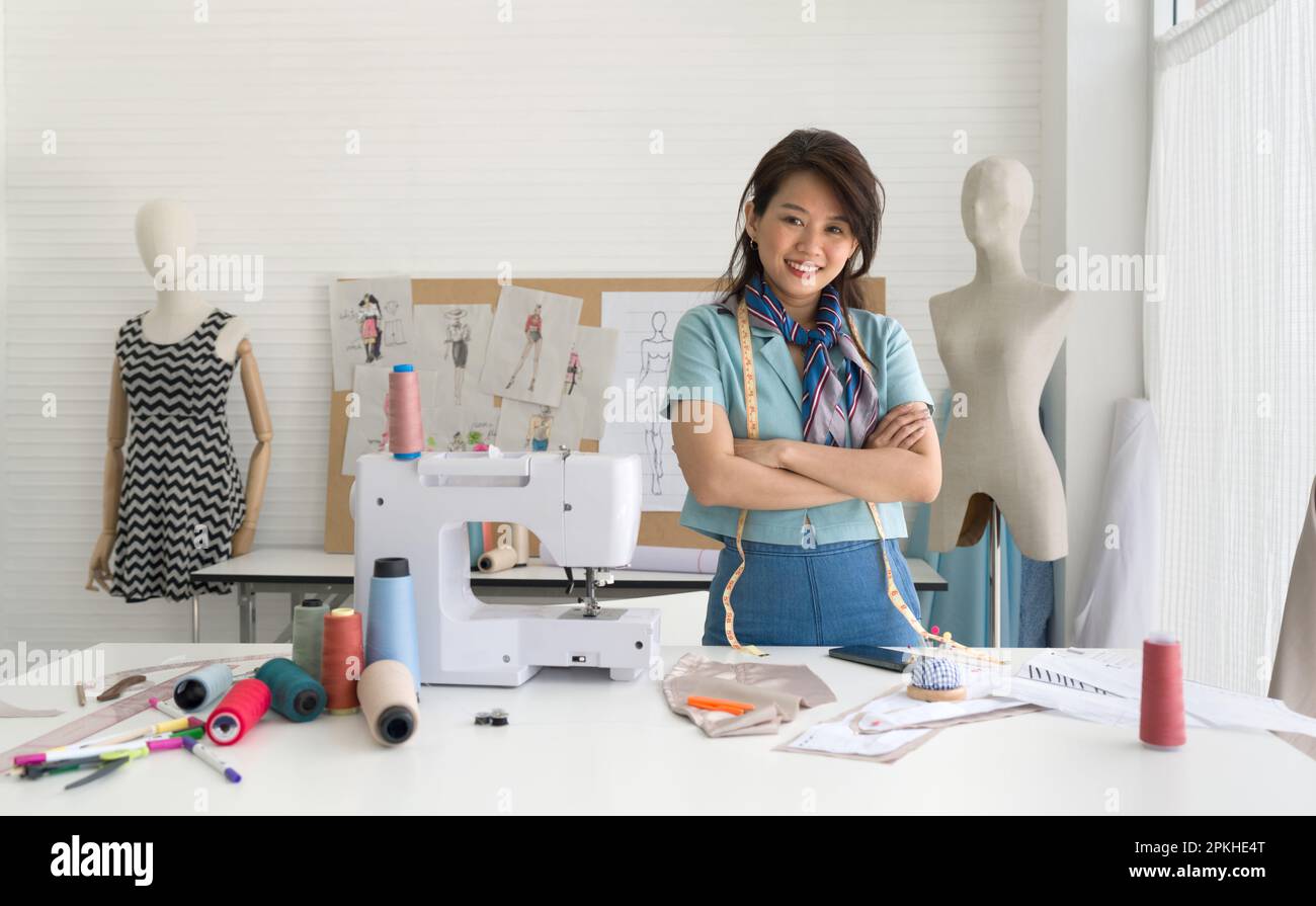Young dressmaker with tape measure stand smiling with arms crossed ...