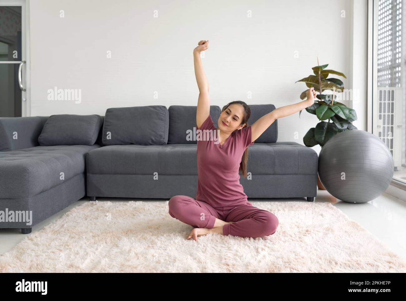 Asian housewife stretching while sitting during home workout on carpet ...