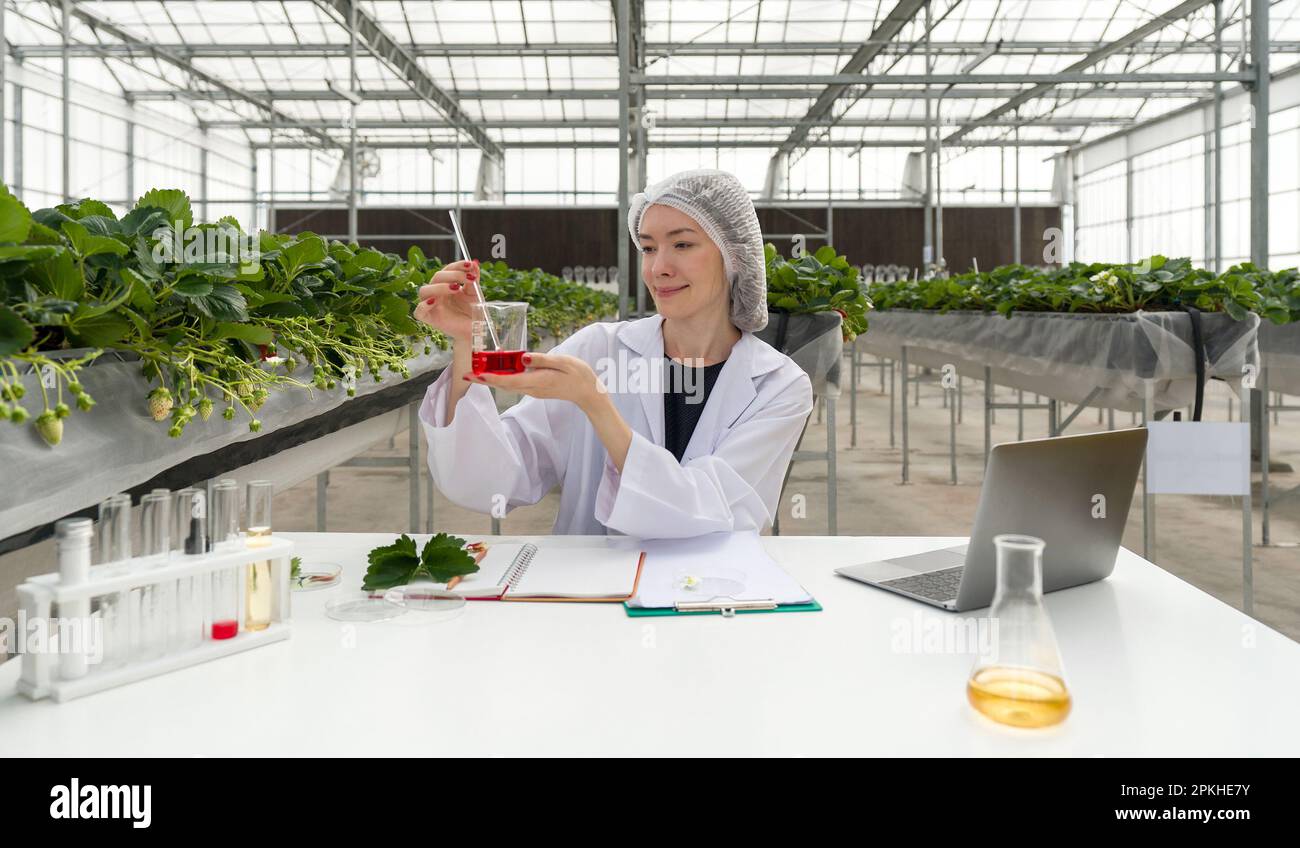 Caucasian female botanical scientist in white gown observes red ...