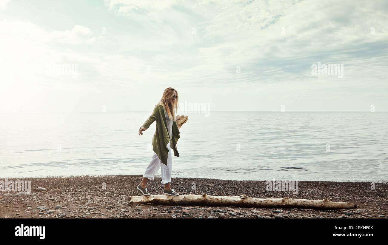 Filling her day with fun. a young woman walking along a log at a lake ...