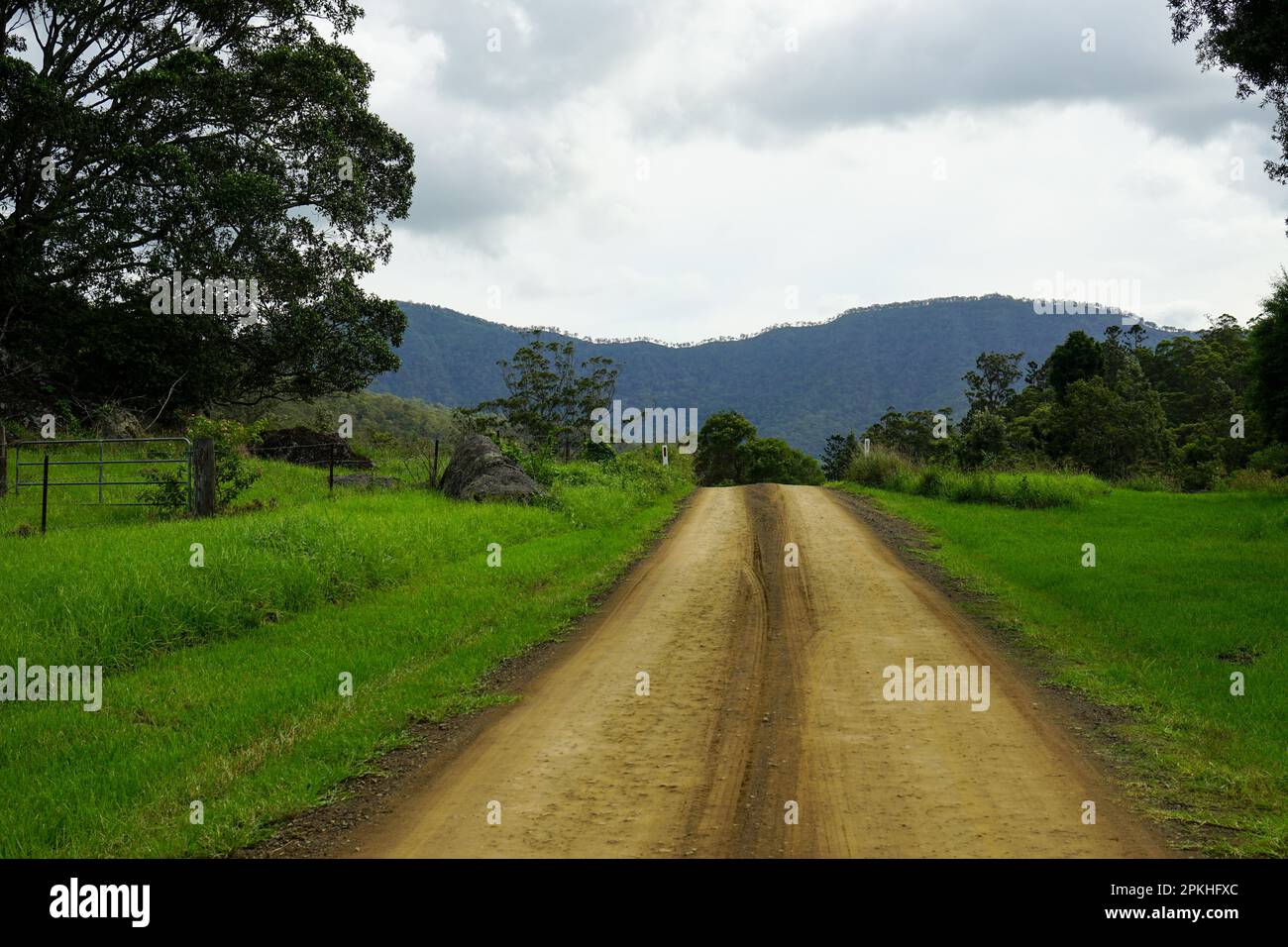 Dirt track on the rise of a hill, with green grass and trees, hill in ...