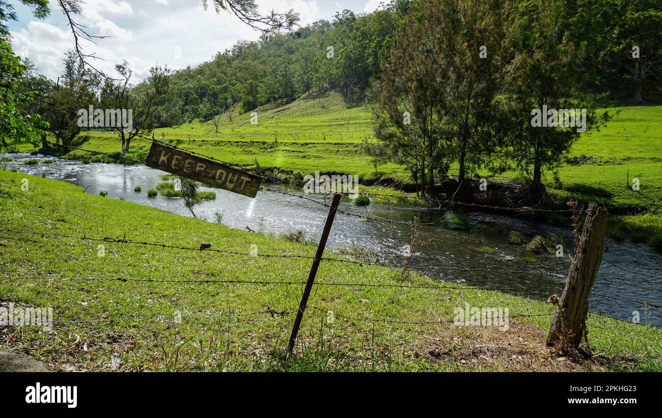 Keep out sign on a barbed wire fence. Creek flowing through a green ...