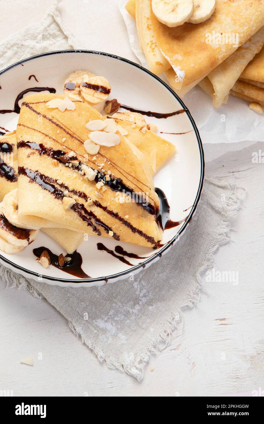 Crepe with banana, chopped almonds and chocolate sauce on white plate ...