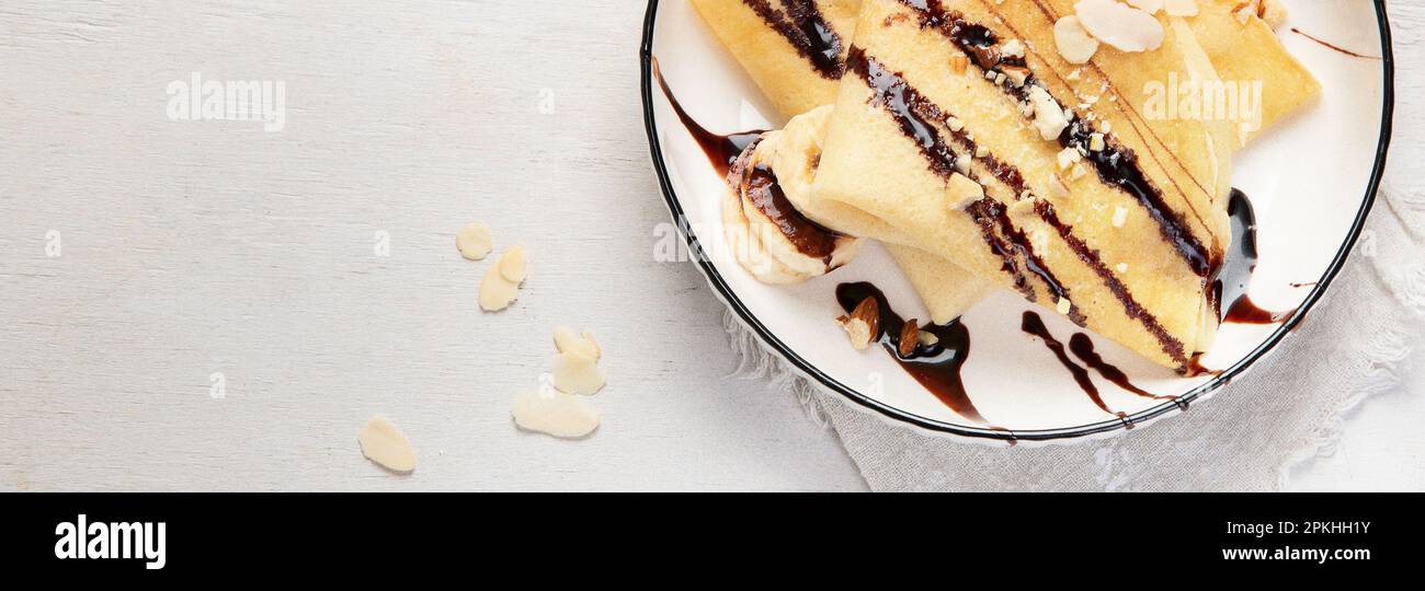 Crepe with banana, chopped almonds and chocolate sauce on white plate ...