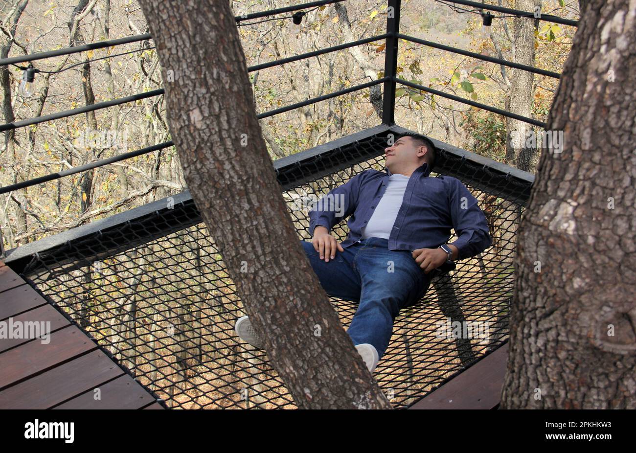 Dark-haired Latino adult man relaxes in a hanging net of a glamping ...