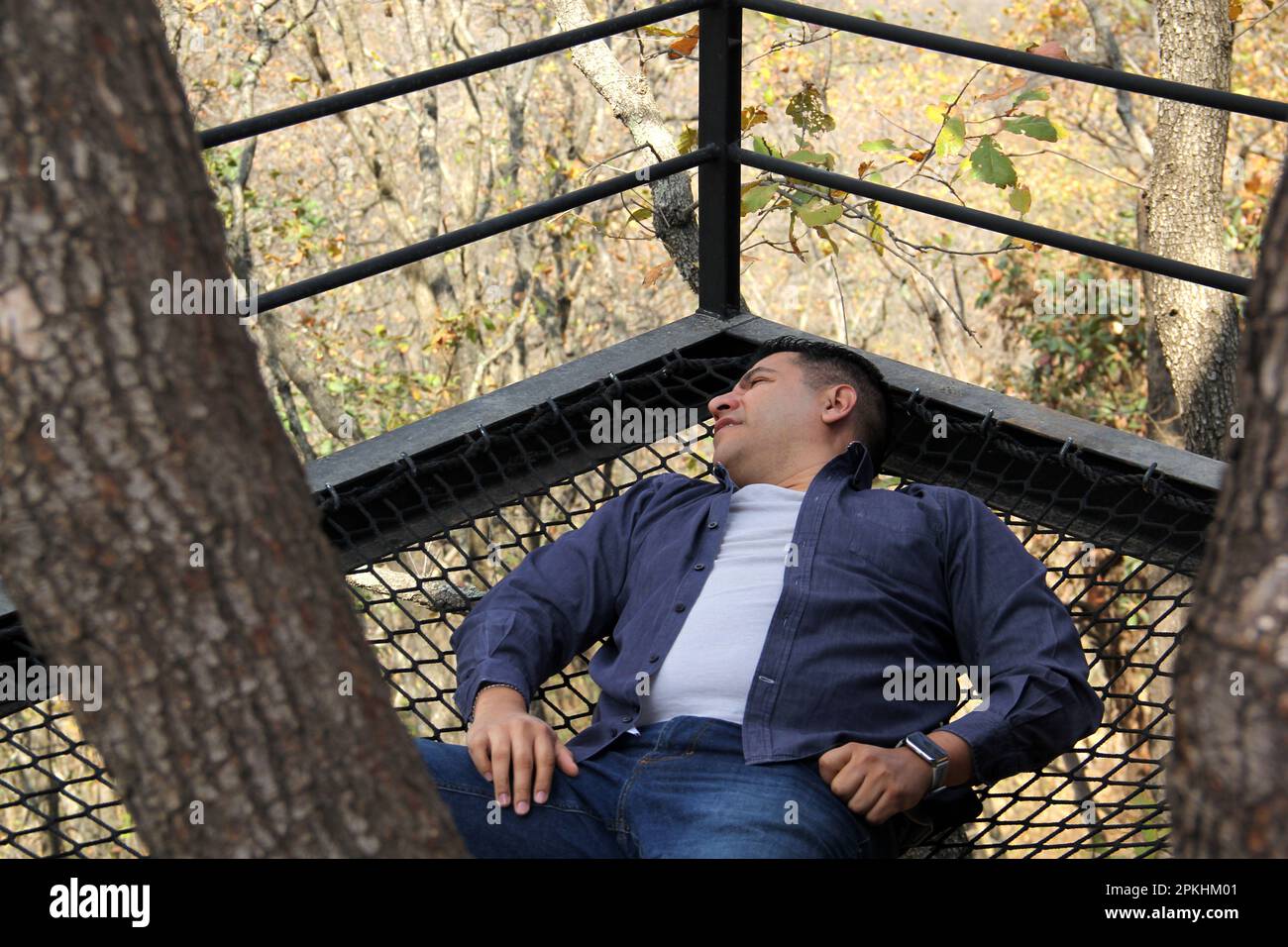 Dark-haired Latino adult man relaxes in a hanging net of a glamping ...