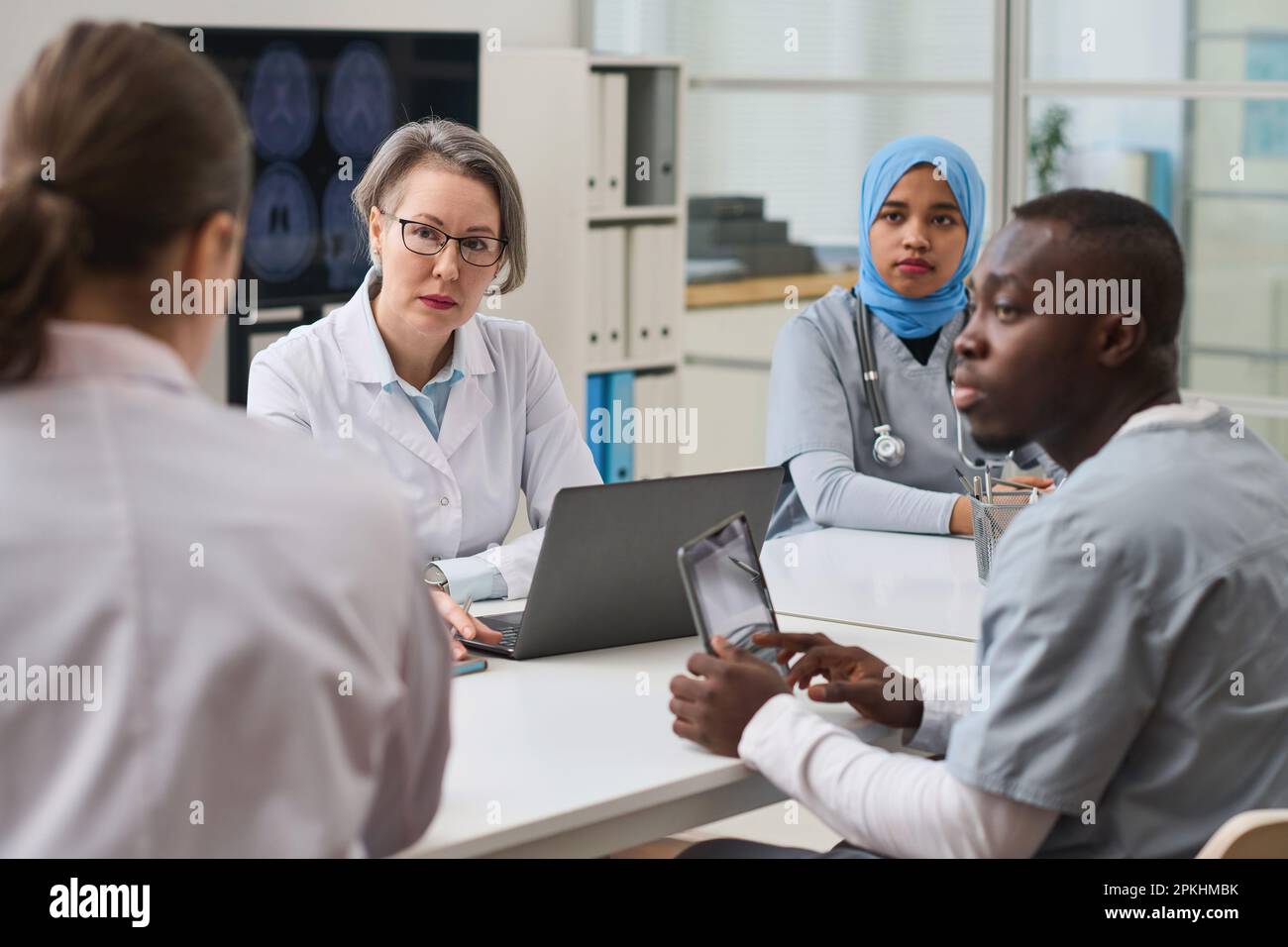 Group of doctors listening to their colleague while using gadgets ...