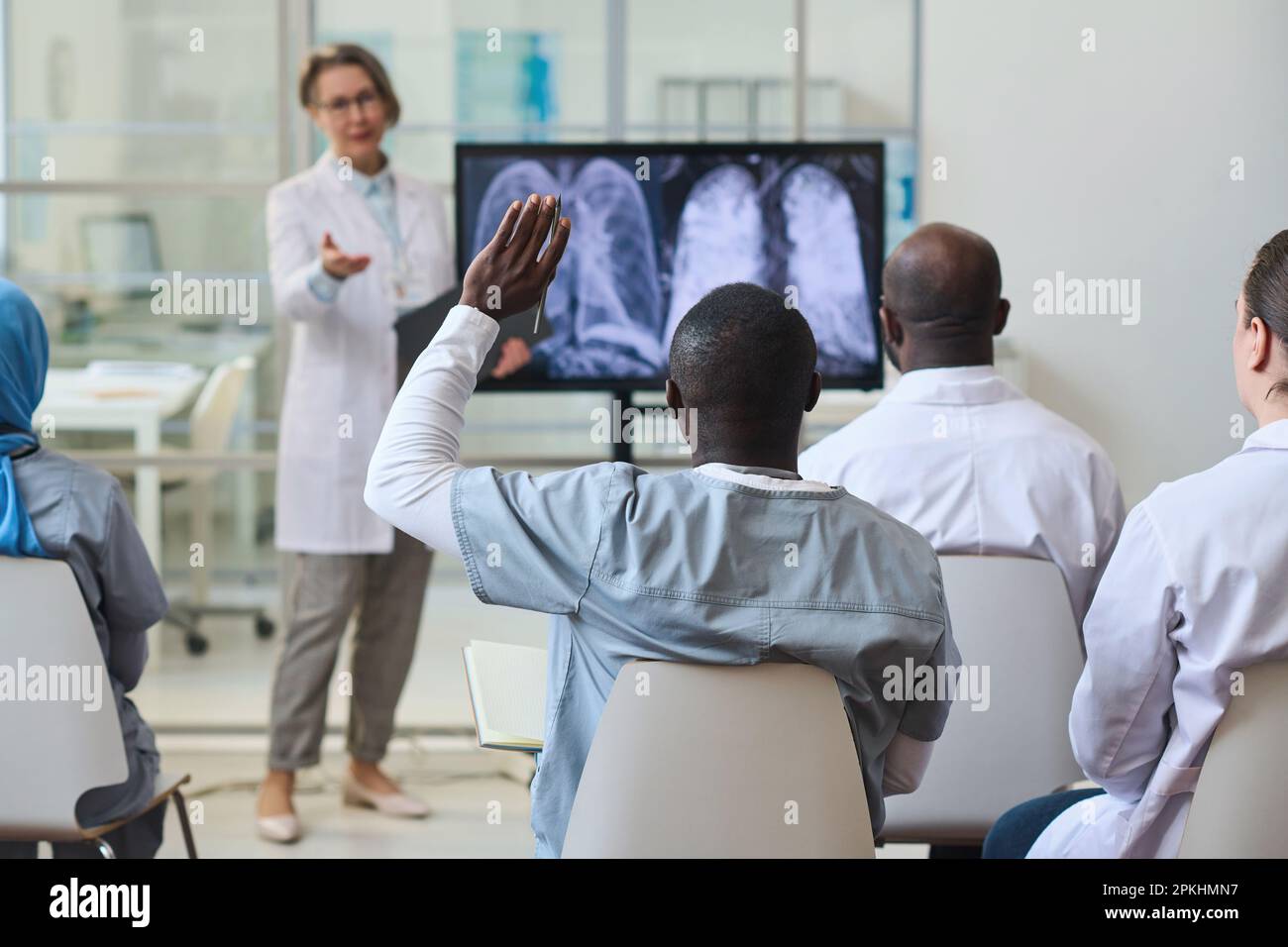 Rear view of group of people asking questions to doctor during medical ...