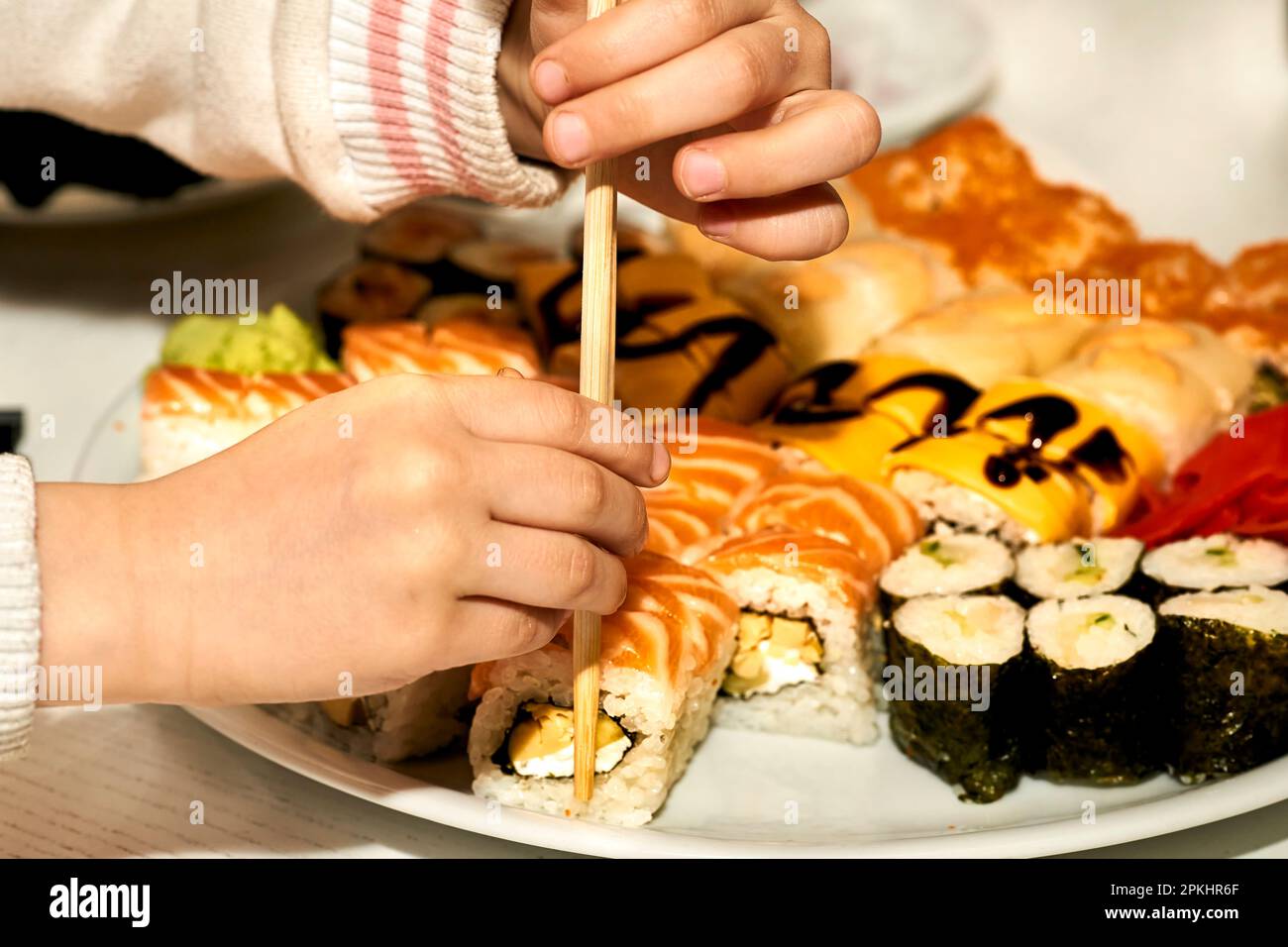 Children's hands taking delicious sushi with chopsticks. The child eats ...