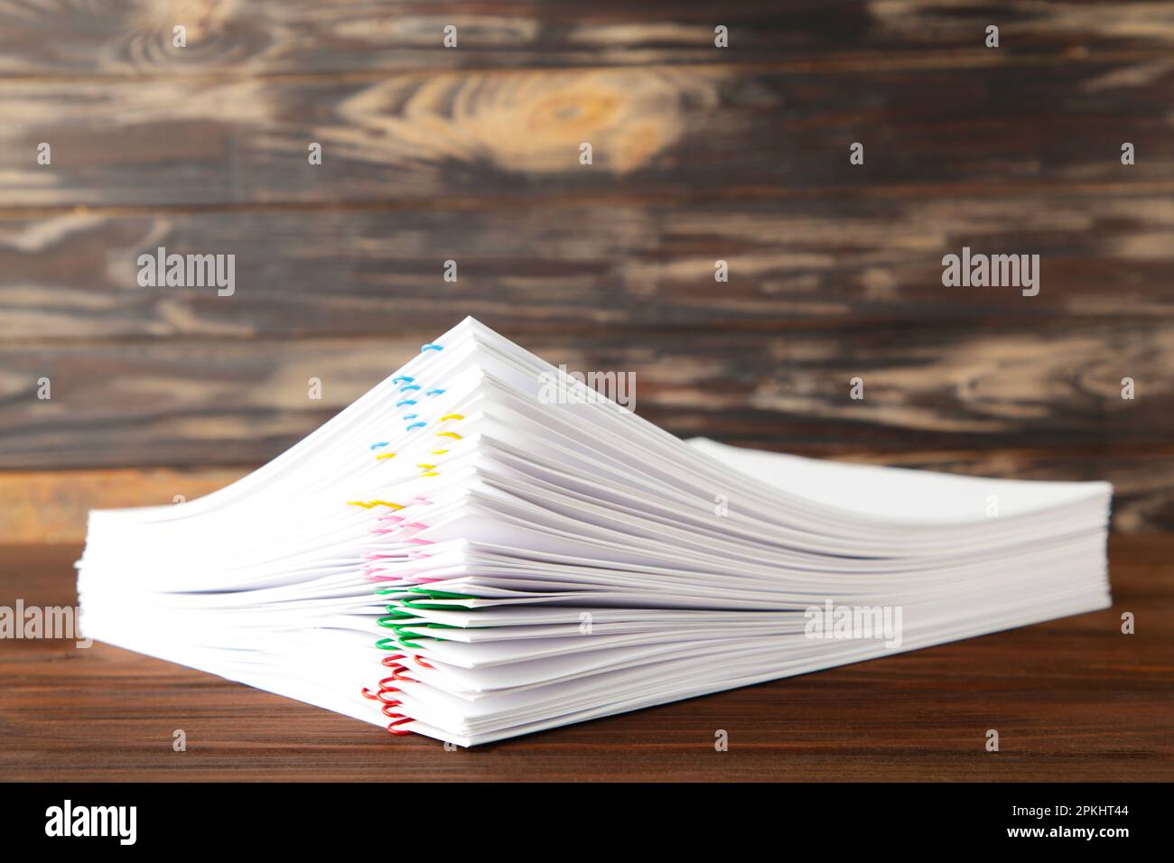 Colorful paper clip with pile of overload white paperwork on brown. Top ...