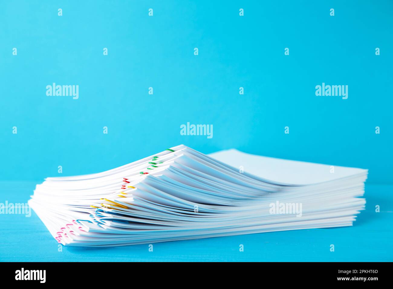 Colorful paper clip with pile of overload white paperwork on blue. Top ...