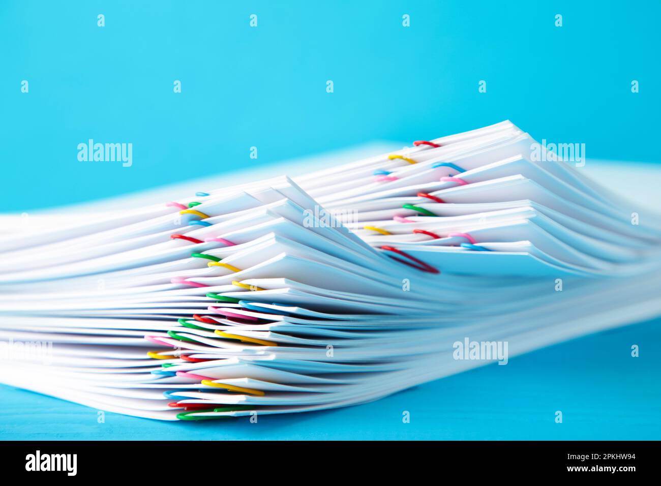Colorful paper clip with pile of overload white paperwork on blue. Top ...