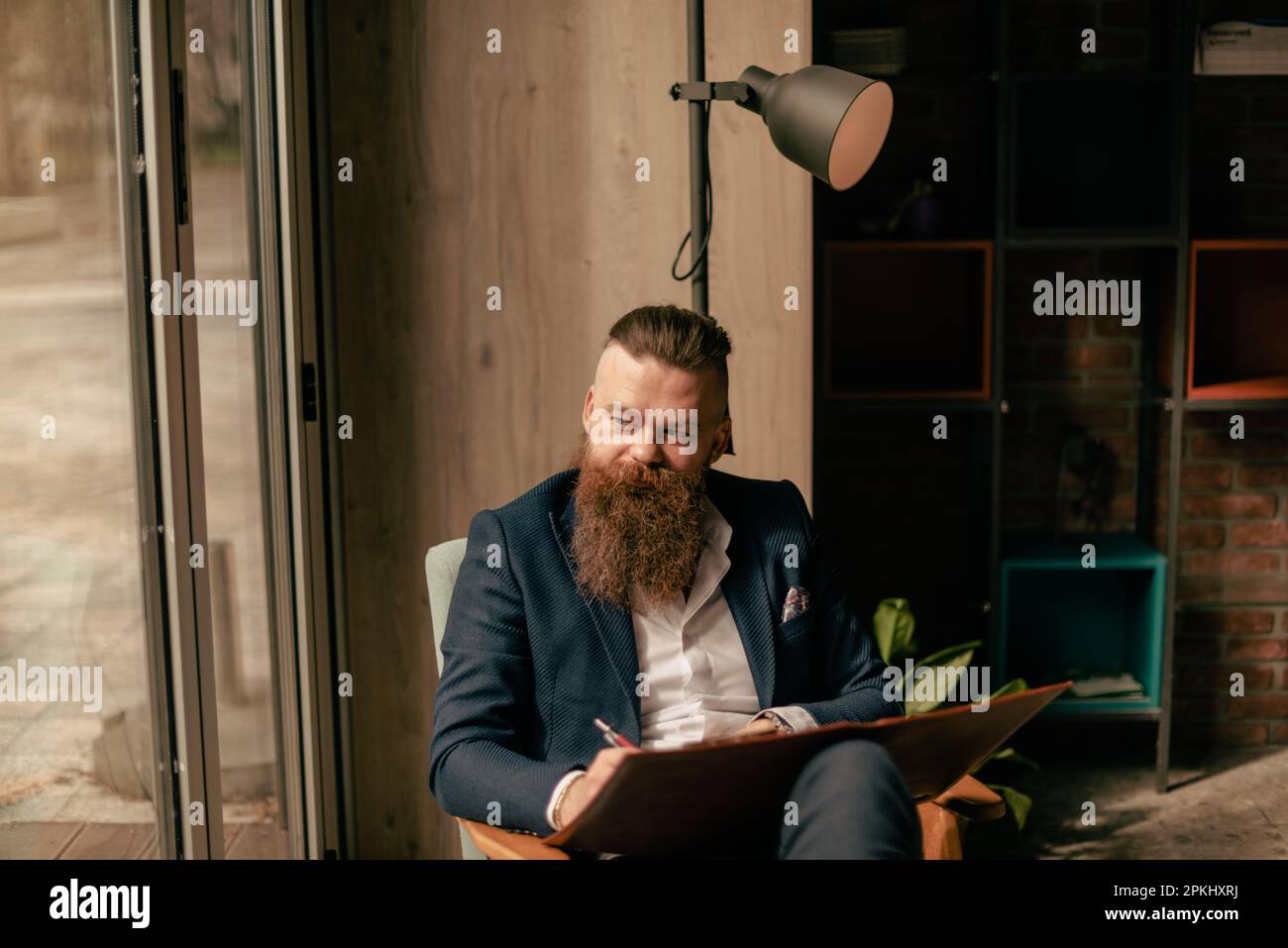 Young bearded man reading and writing in his notebook sitting with his ...
