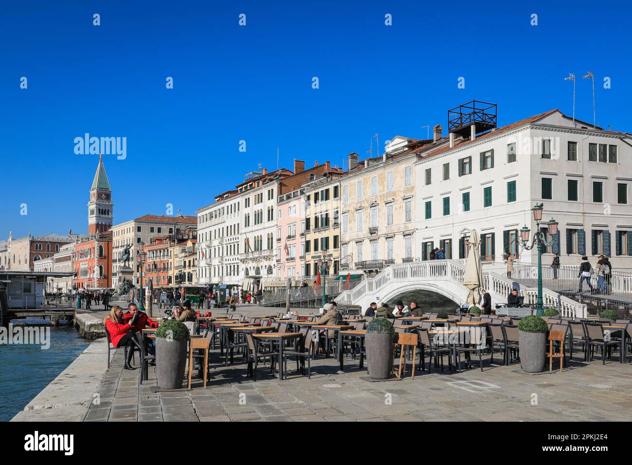 Venice canal waterside promenade, people in cafes, blue sky and ...