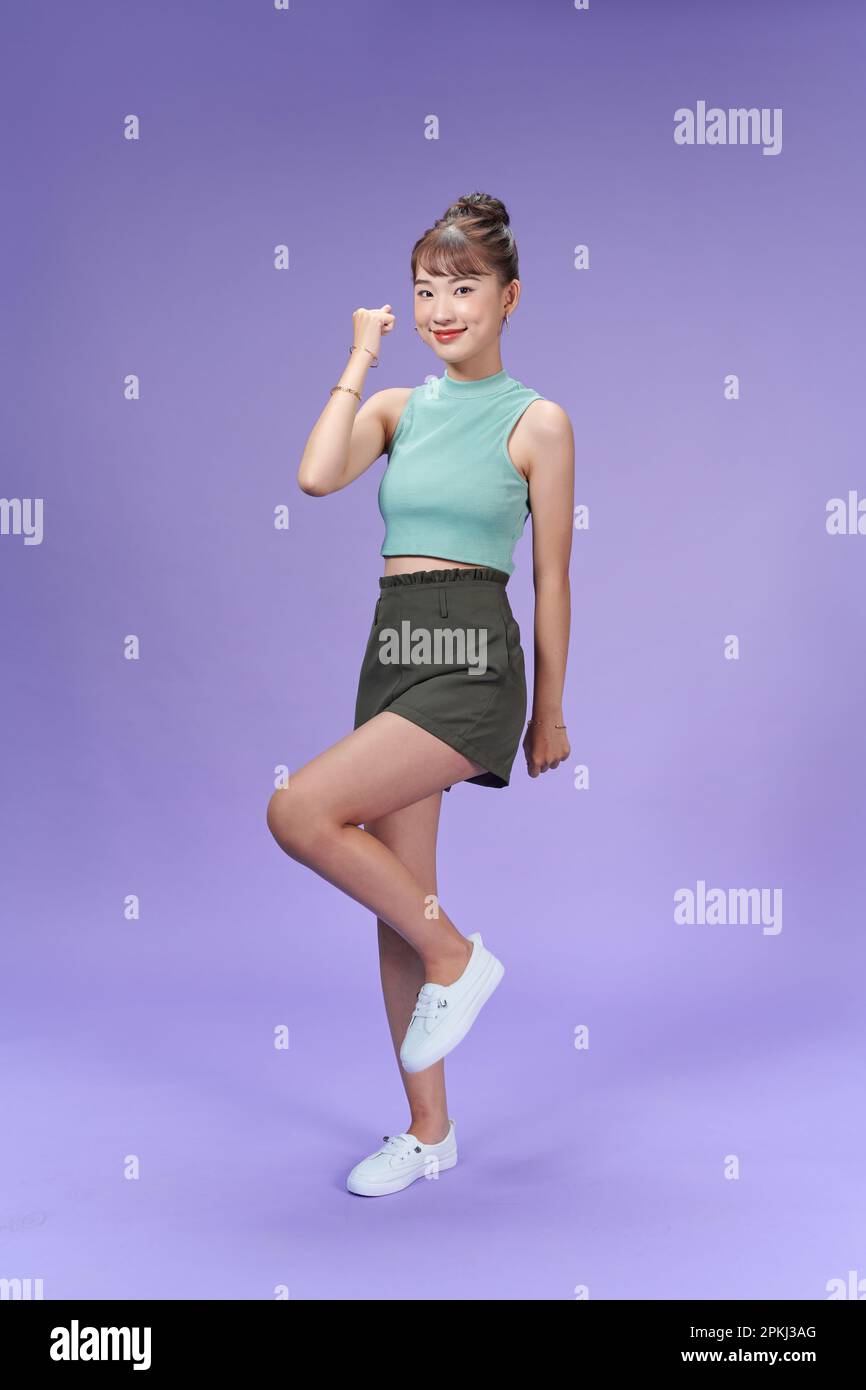 Full length view of blissful asian girl dancing on purple background ...
