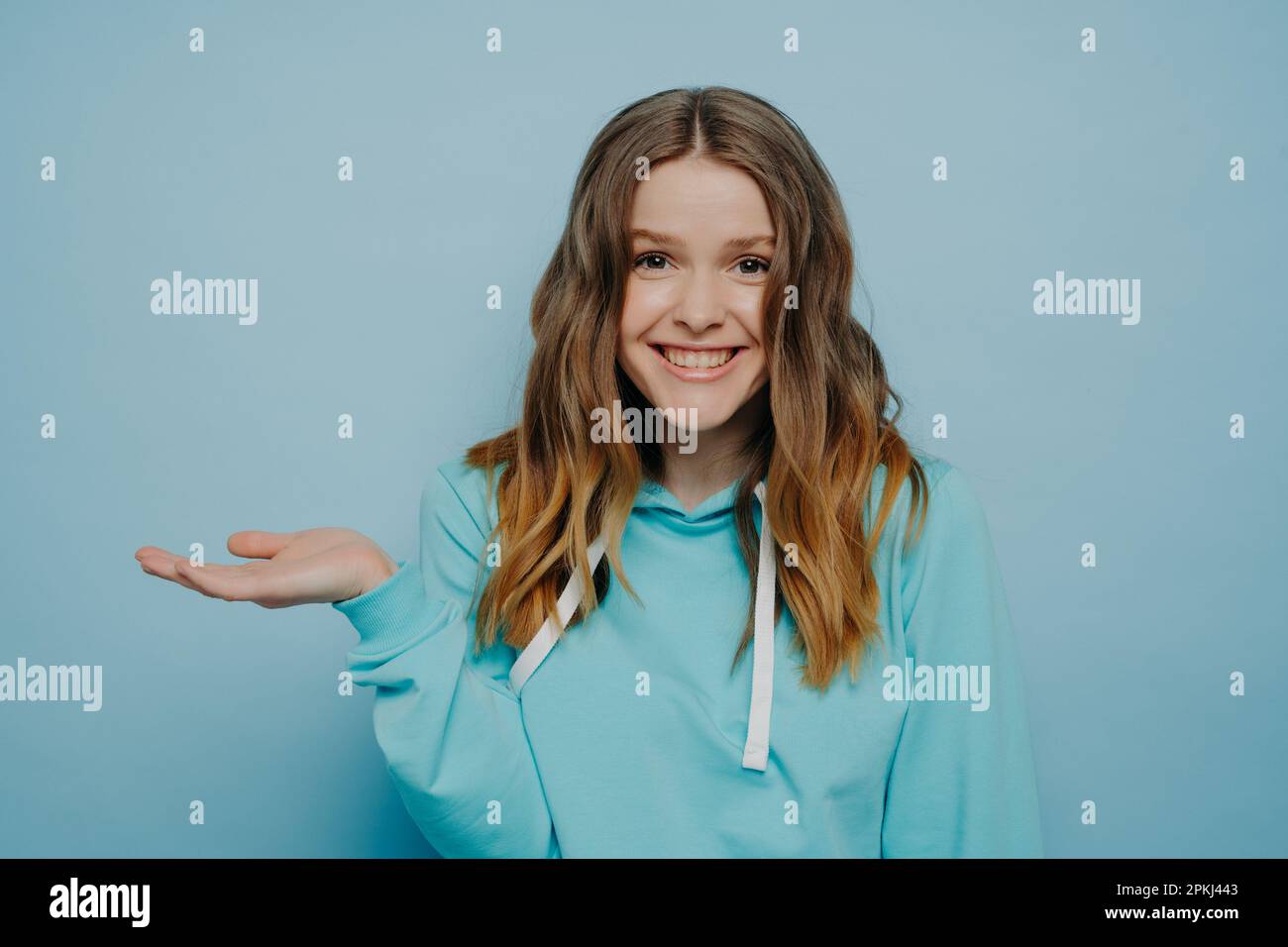 Smiling teenage girl with tipping hand shrugging shoulders standing ...