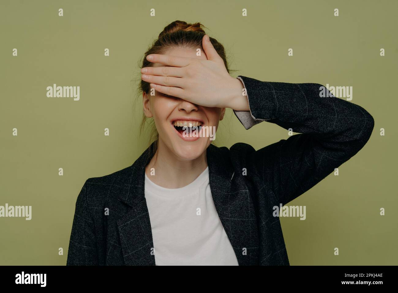 Laughing young female in casual clothes covering eyes with hand while ...