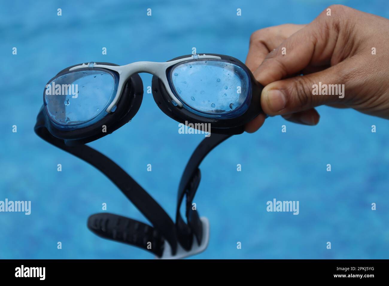 Kids swimming goggles held in hand with a pool on the background ...