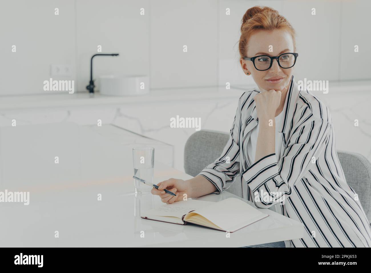 Thoughtful redhead woman distracted from work makes notes in notepad ...