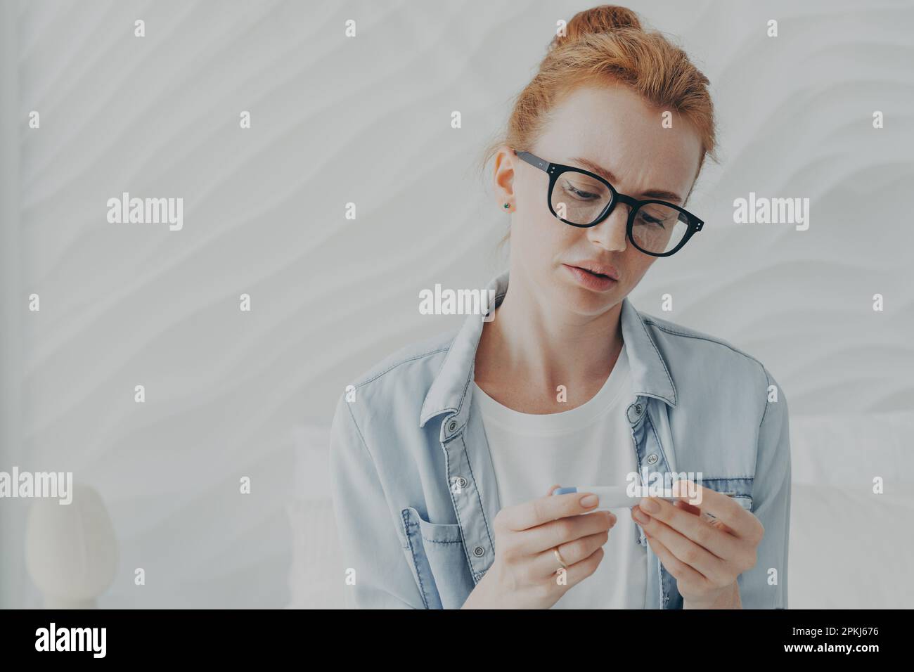 Upset sick young woman having high fever, holding thermometer while ...