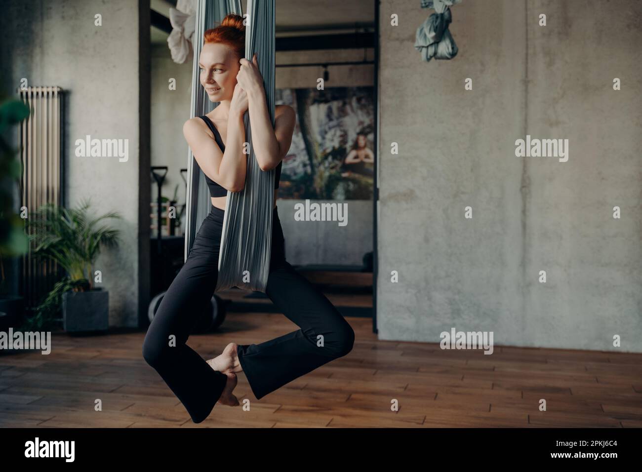 Full length of young slender woman with red hair practices anti gravity ...