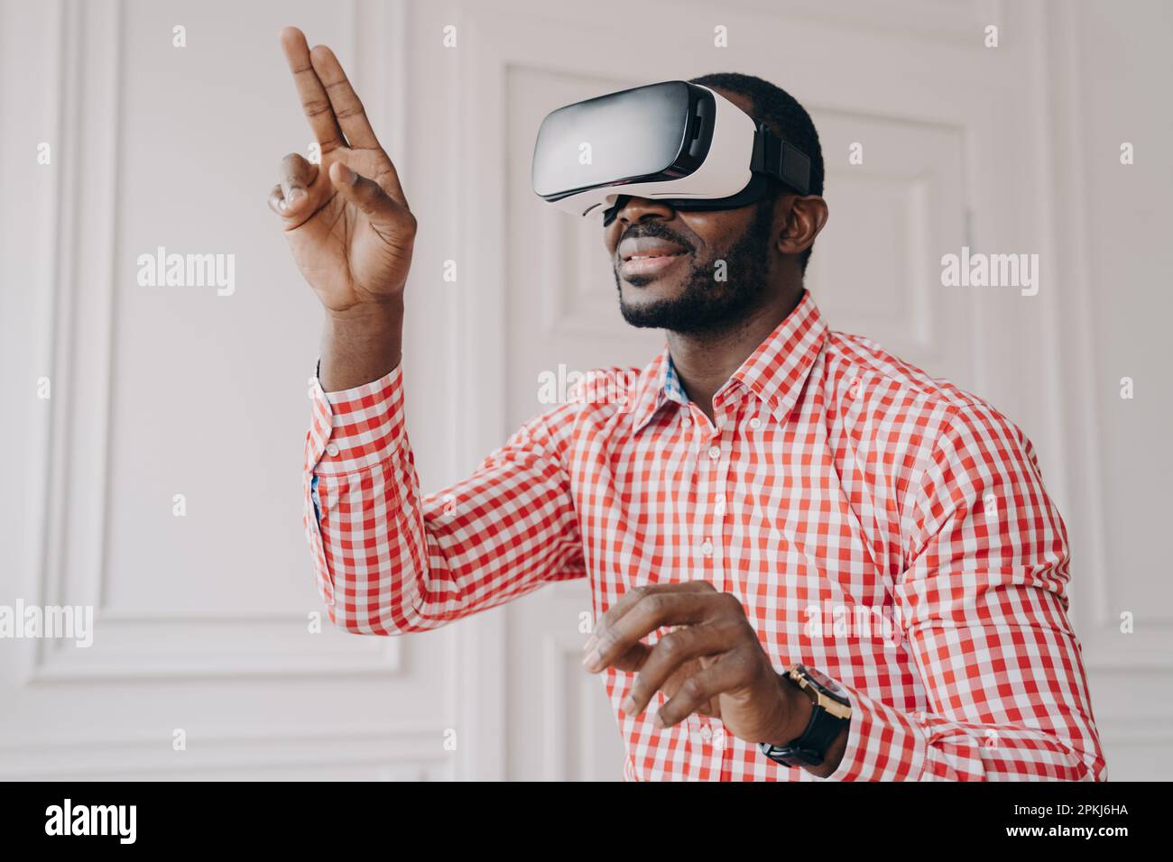 Enthusiastic smiling african ethnicity guy in VR headset glasses enjoying virtual reality online ...