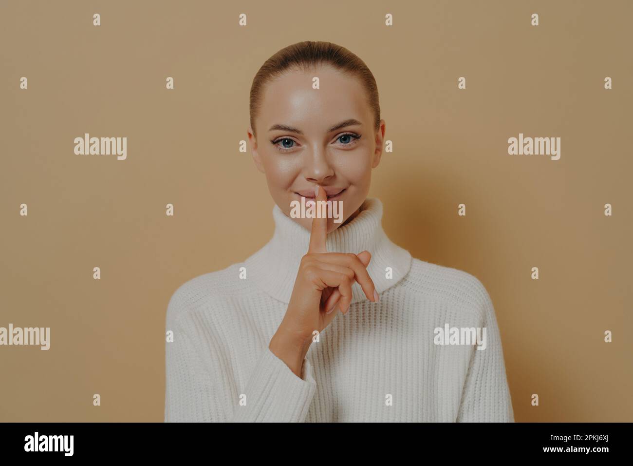 Keep it secret. Young attractive smiling lady wearing white knitted ...
