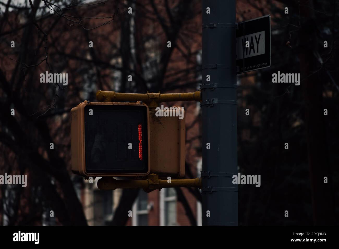 A traffic signal is mounted on a metal pole beside a brick facade of a ...