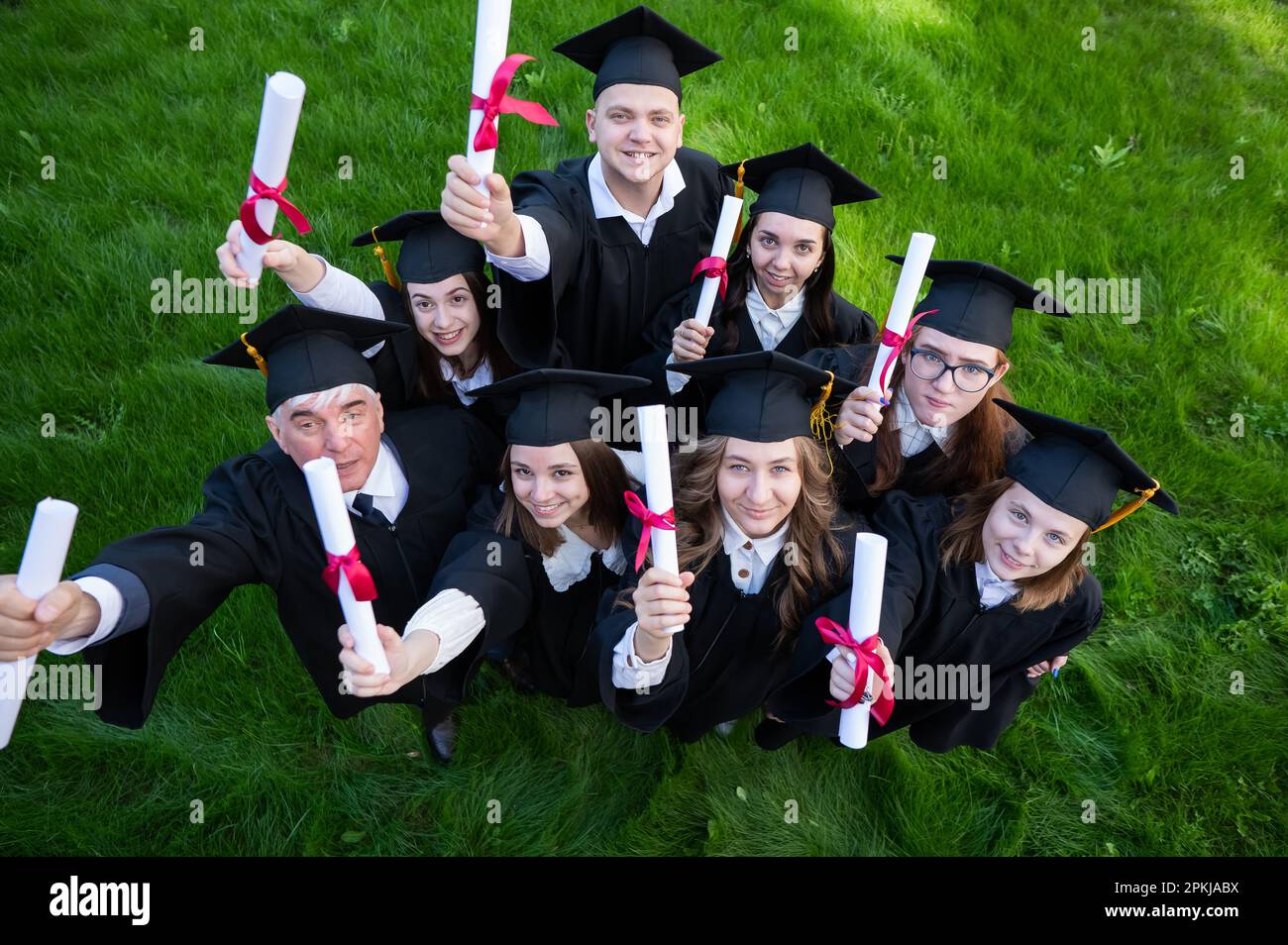 Graduates in robes show off their diplomas outdoors. View from above ...