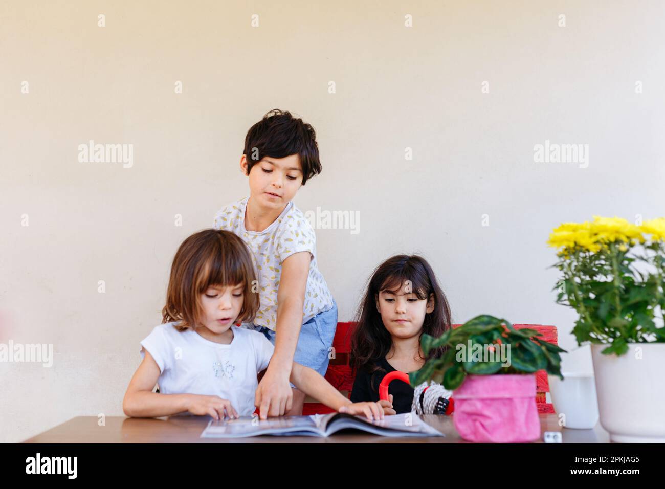 three children sitting outside and watching magazine Stock Photo - Alamy