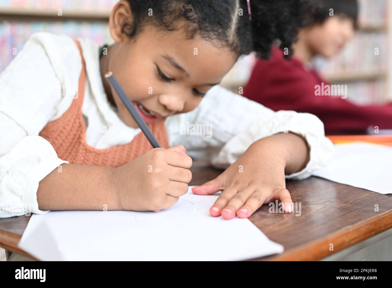 Cute pupils writing and painting on paper at desk in classroom Stock ...