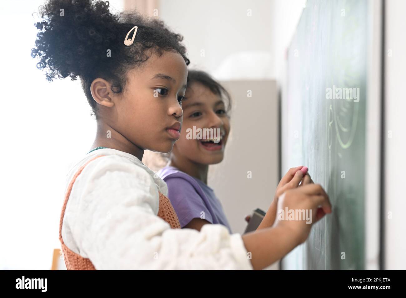 Happy girls pupils writing on blackboard in classroom at school Stock ...