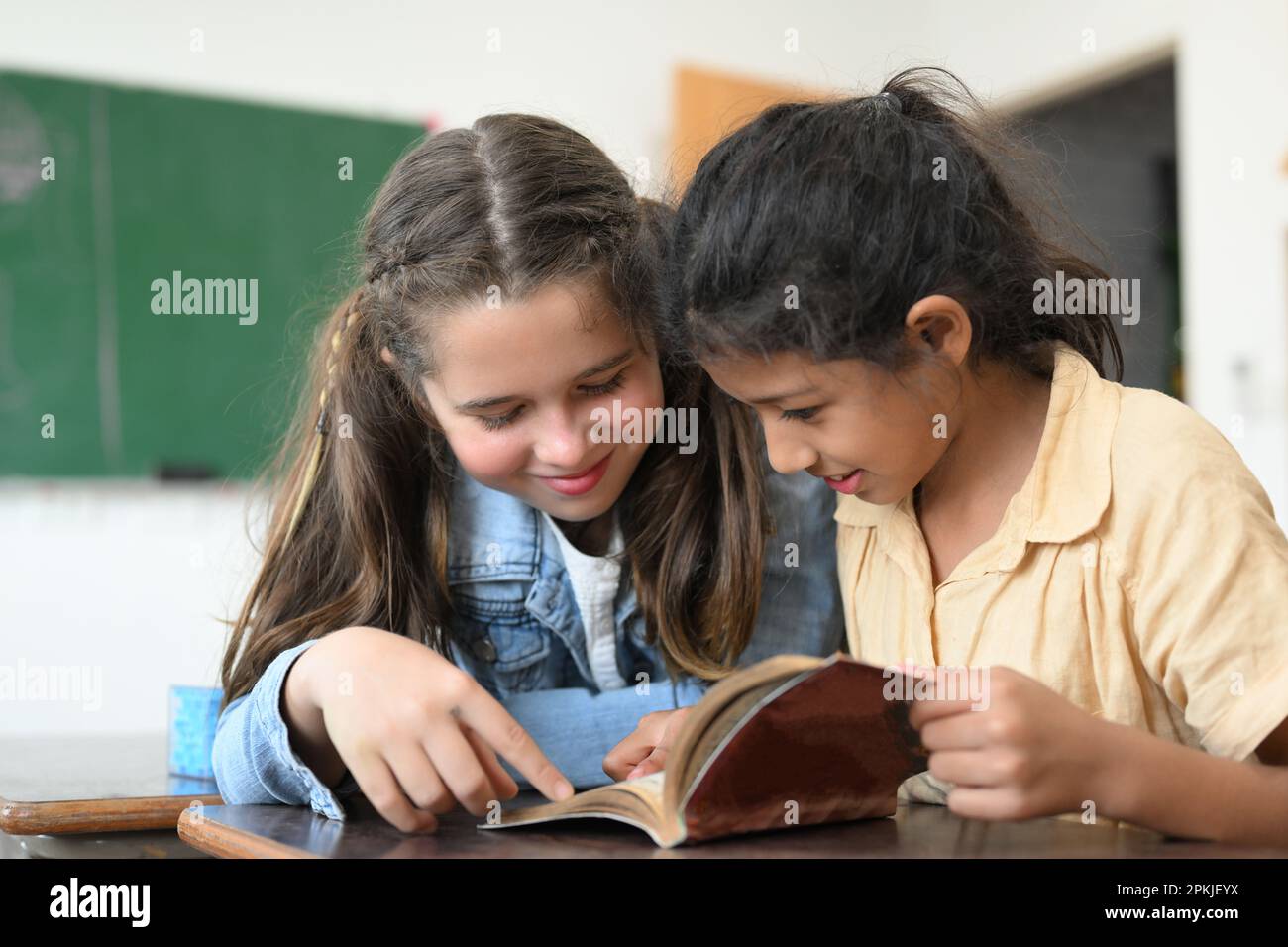 Cheerful students reading book on desk in classroom at school Stock ...