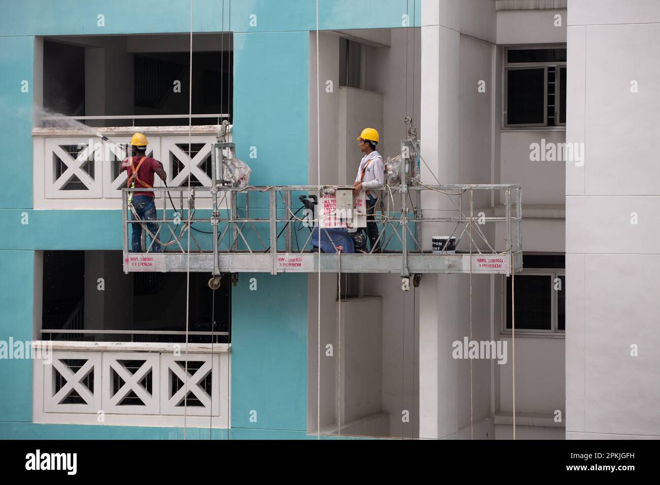 Two workers on scaffold elevator, one working using water jet to clean ...