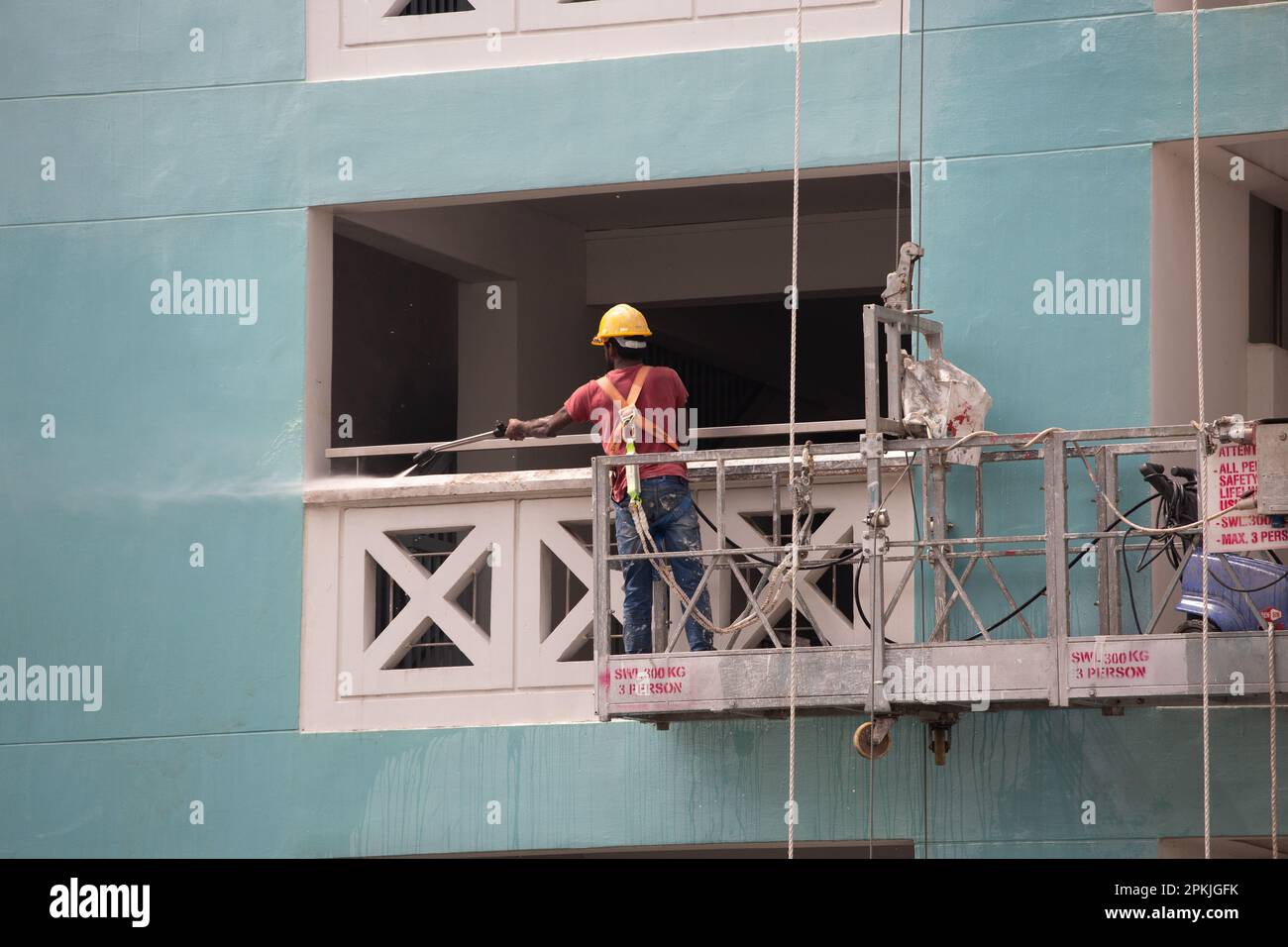 Worker on scaffold elevator using water jet to clean off the dirt of ...