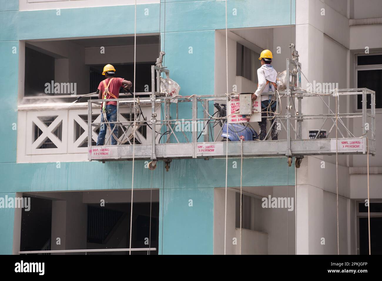 Two workers on scaffold elevator, one working using water jet to clean ...