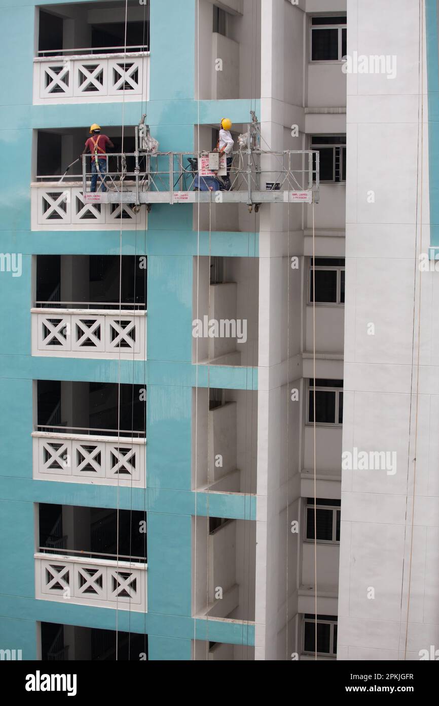 Two workers on scaffold elevator, one working using water jet to clean ...