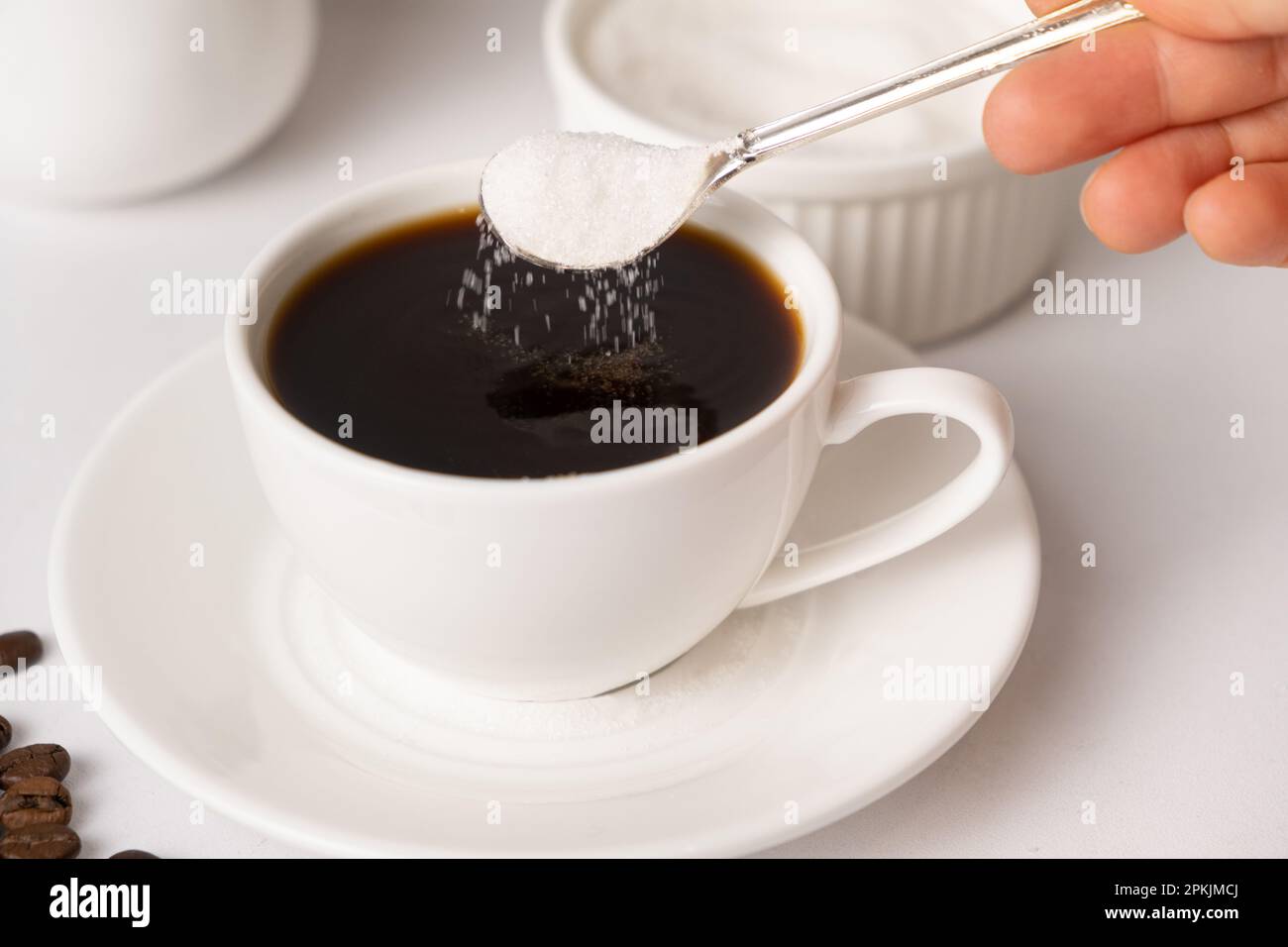 The process of pouring white sugar from a spoon into a white cup of ...