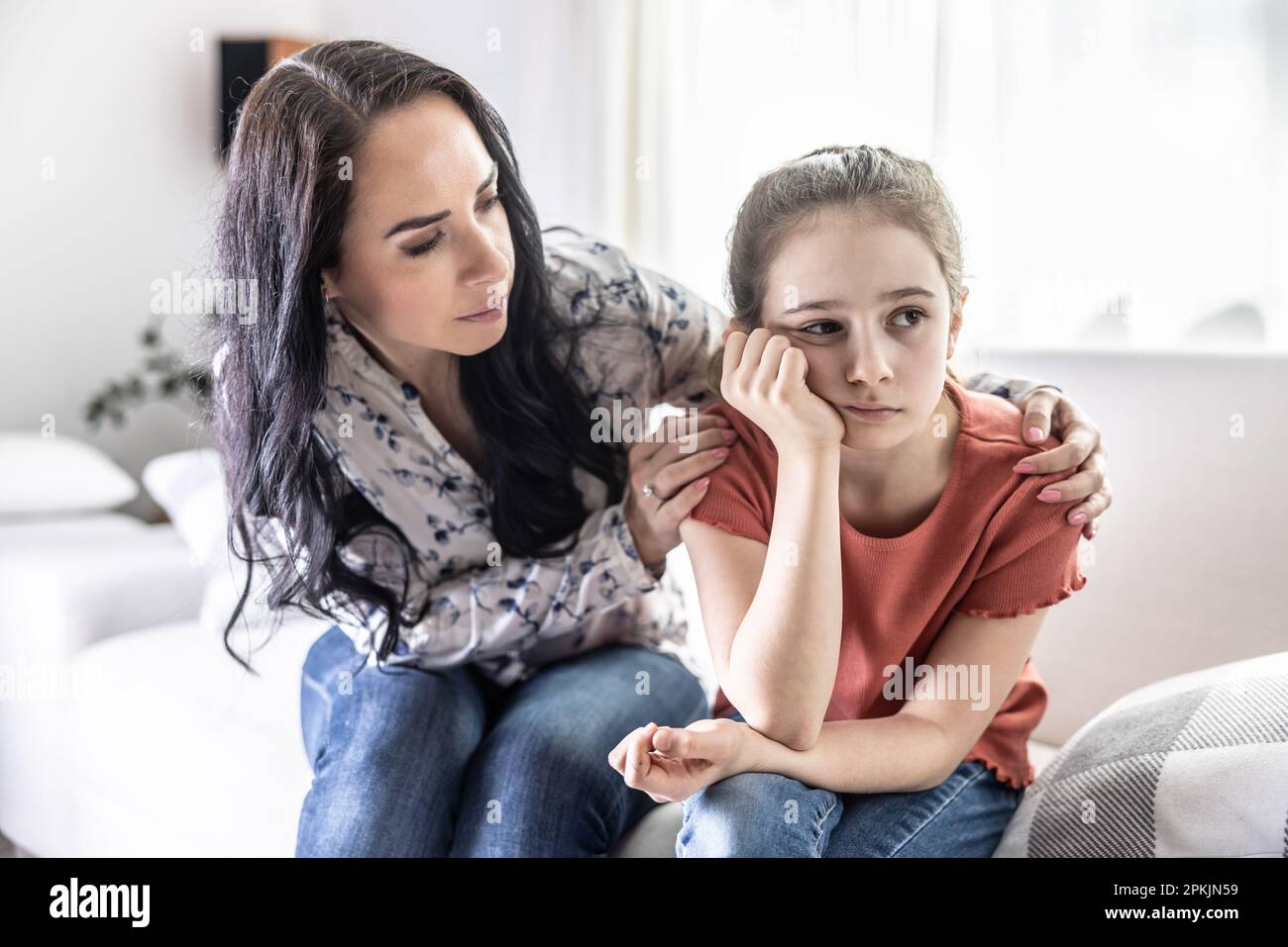 Offended young daughter sulks on a couch while her mother tries to talk ...