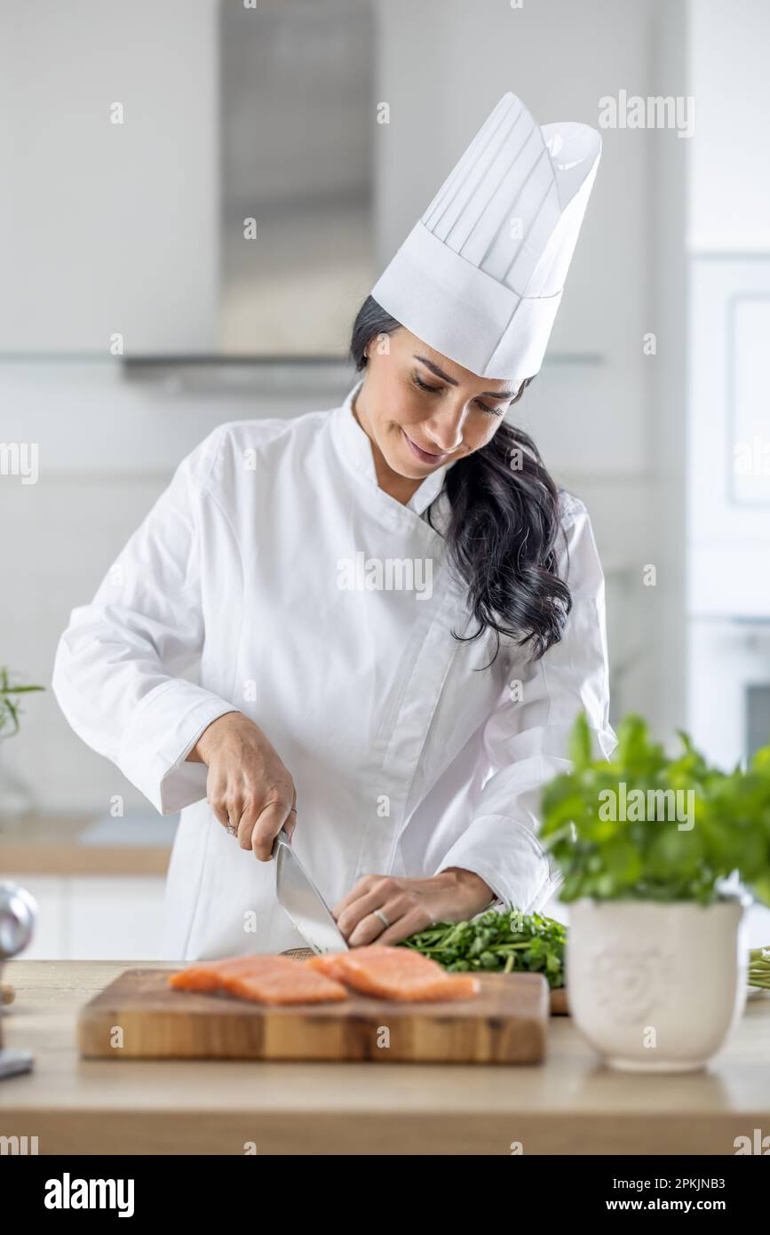 Woman working as a chef smiles as she cuts raw fish in the restaurant ...