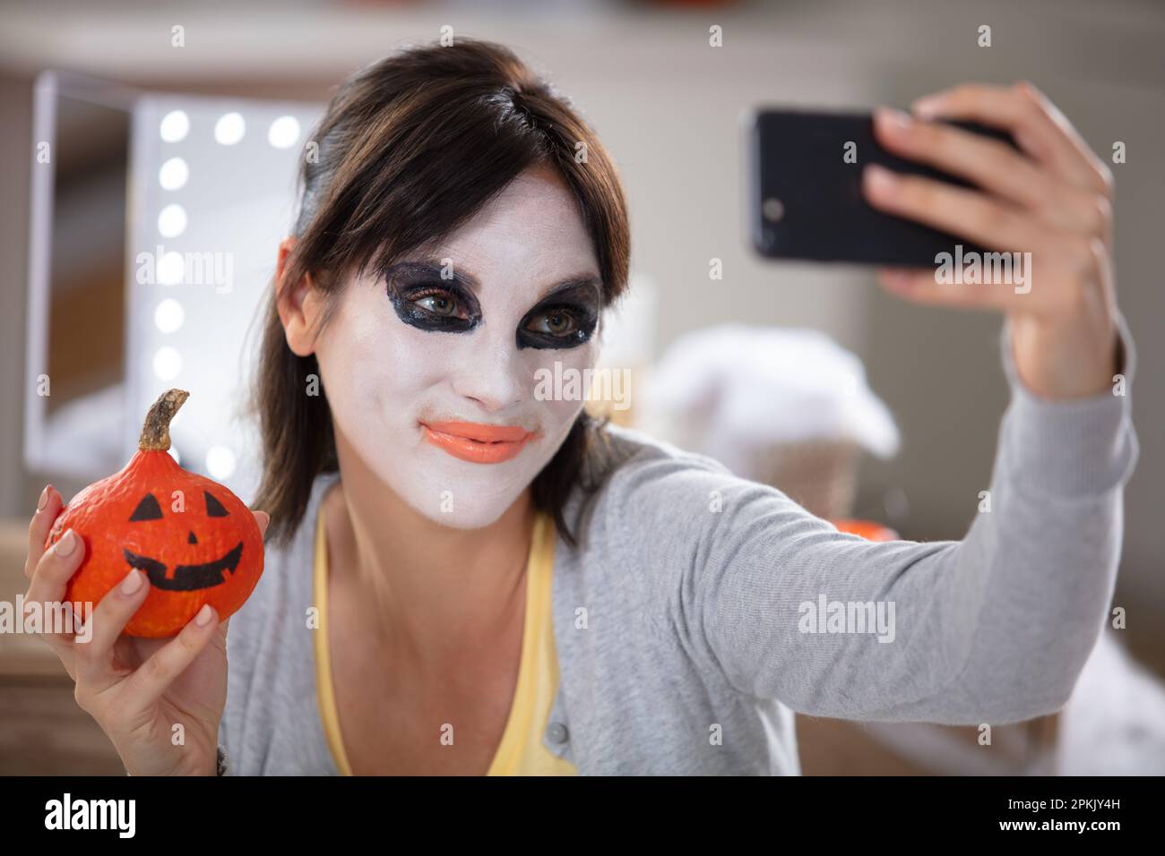 woman wearing face-paint taking a halloween selfie holding pumpkin ...