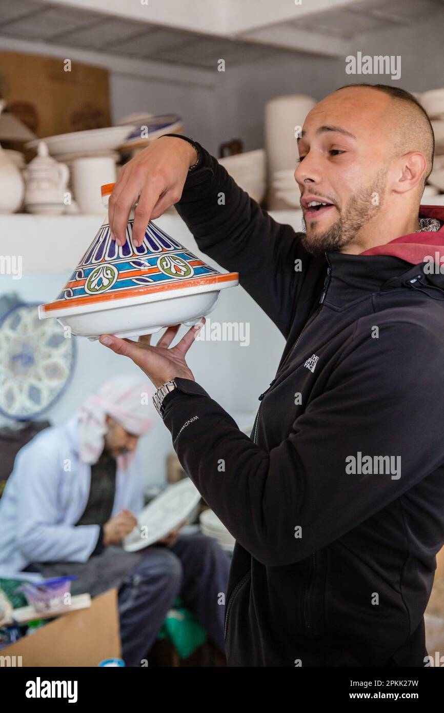 A man displays a handpainted tagline while another man paints a ceramic ...