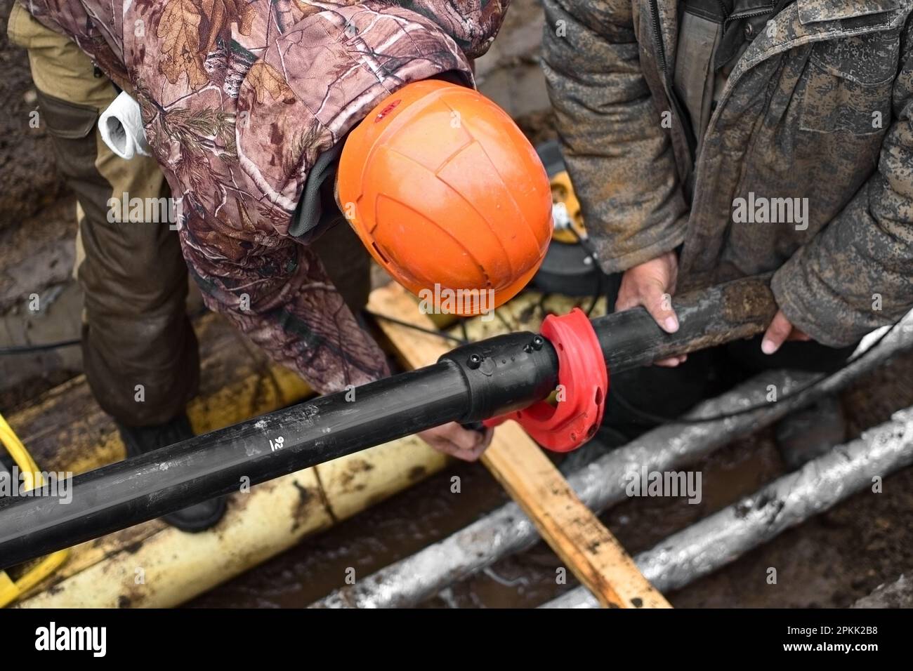 Worker in helmet repairs communal water pipe in trench on street. Work ...