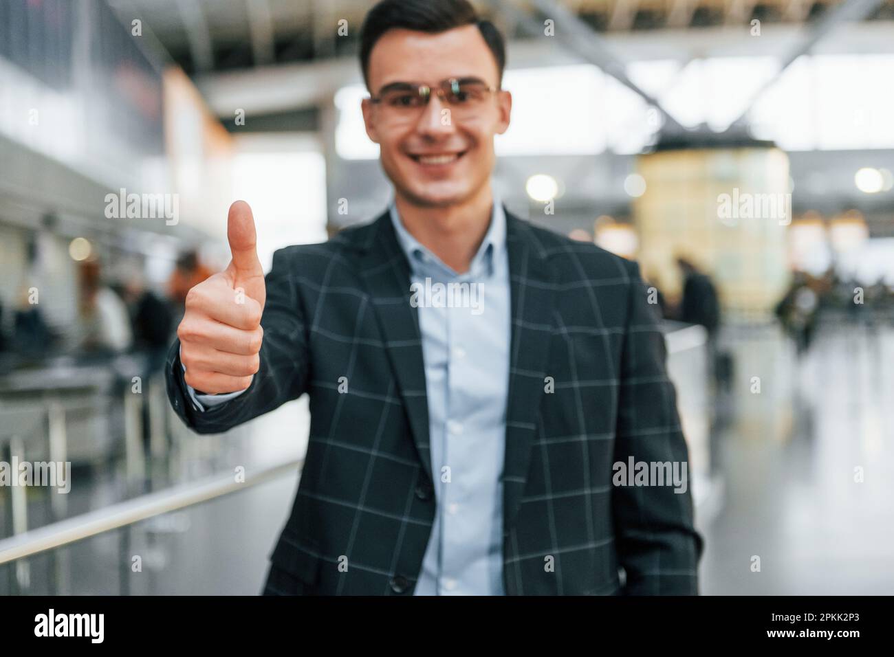 Showing thumb up. Young businessman in formal clothes is in the airport ...