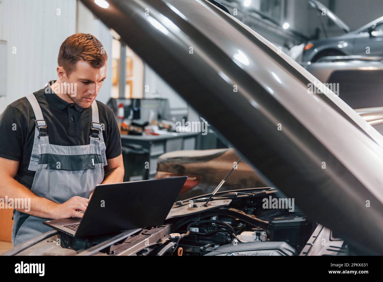 Using laptop. Man in uniform is working in the auto service Stock Photo ...